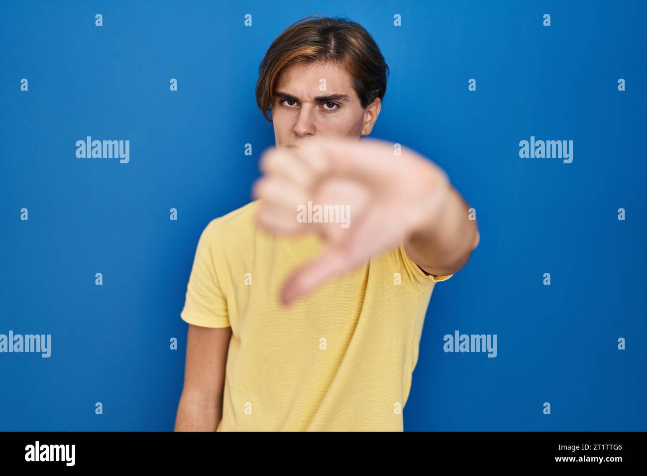 Young man standing over blue background looking unhappy and angry ...