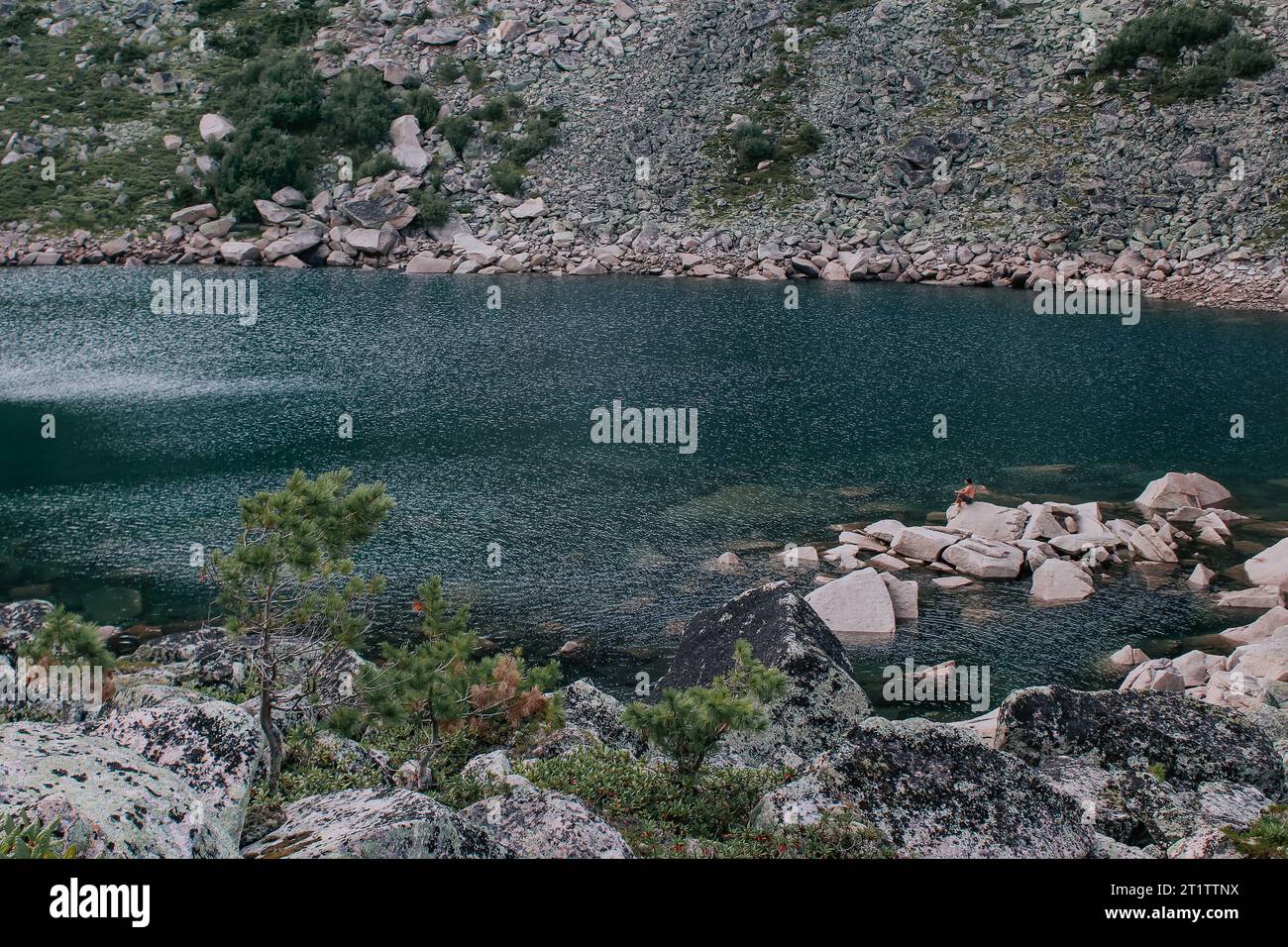Water ripples in a green mountain lake. Man sits on stone sticking out ...