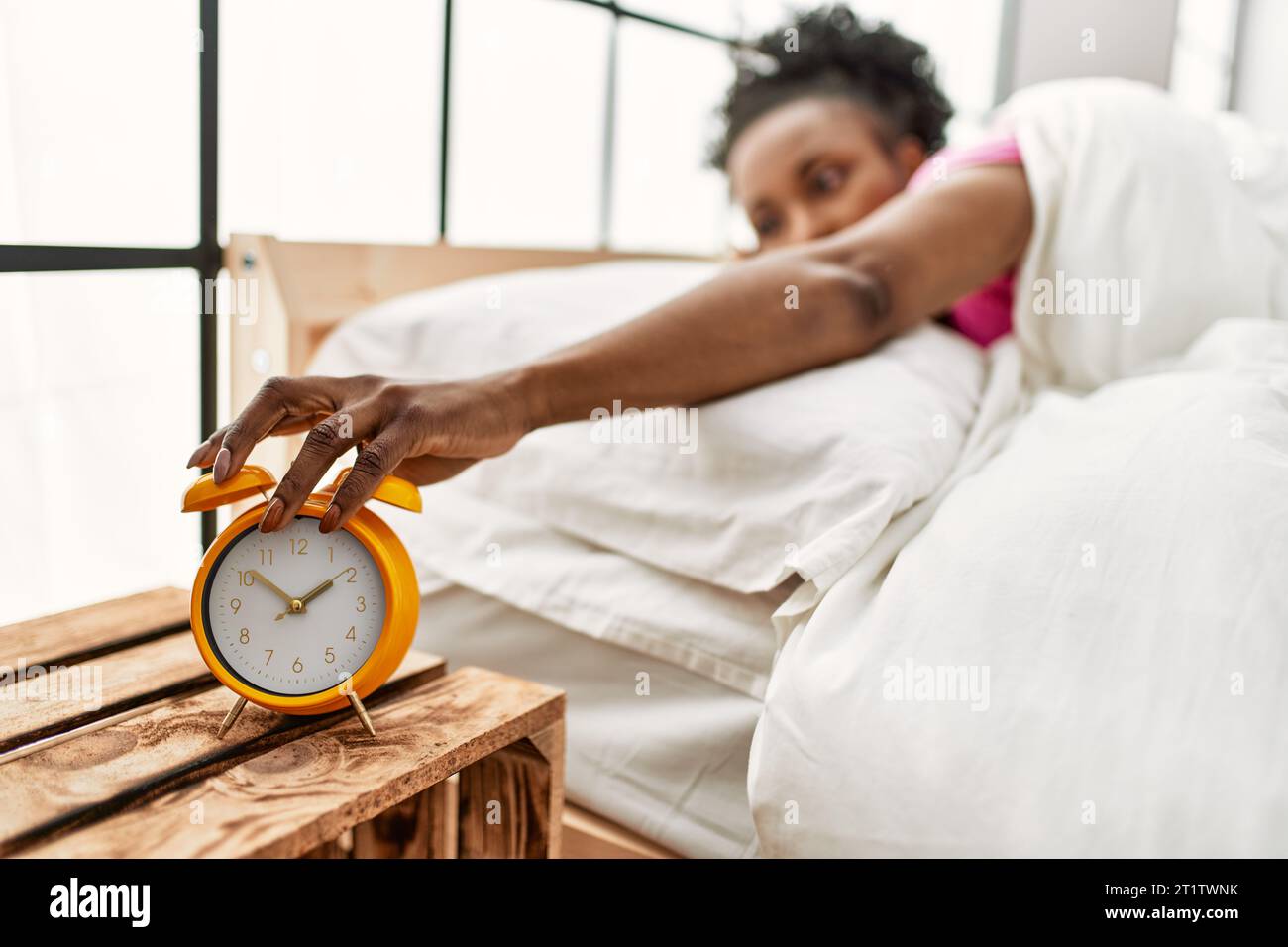 African american woman turning off alarm clock lying on bed at bedroom ...