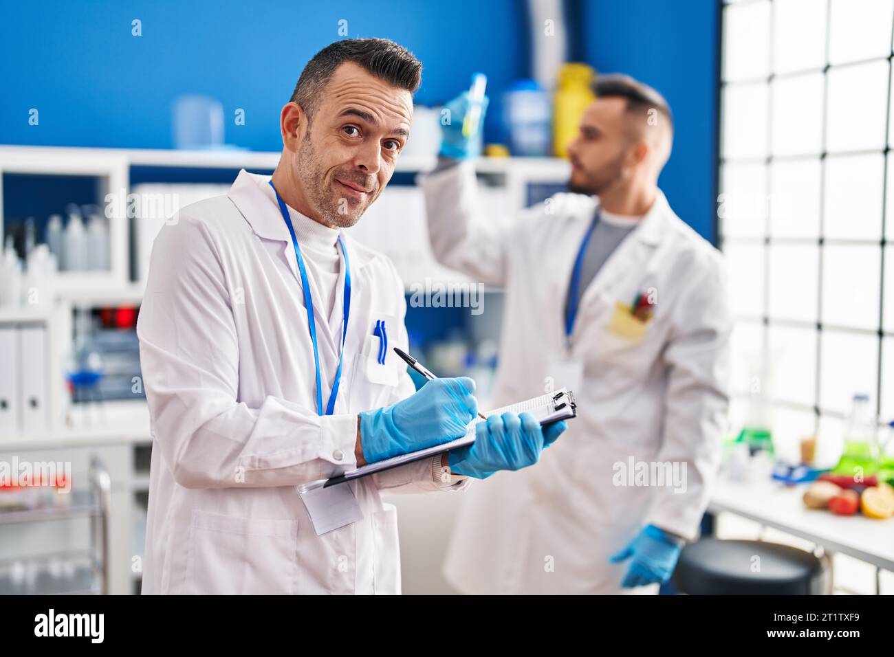Two men scientists writing on document holding test tube at laboratory ...