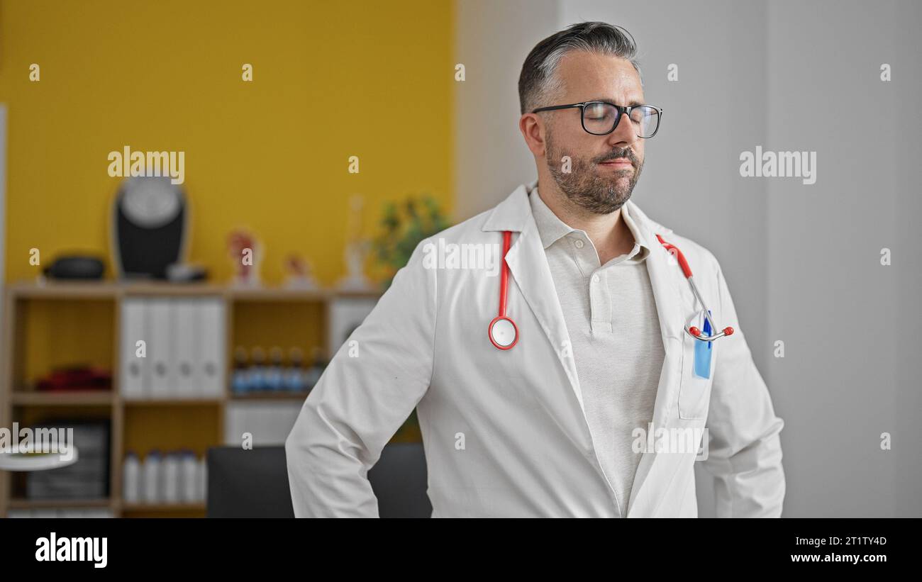 Grey-haired man doctor standing with serious expression at the clinic ...