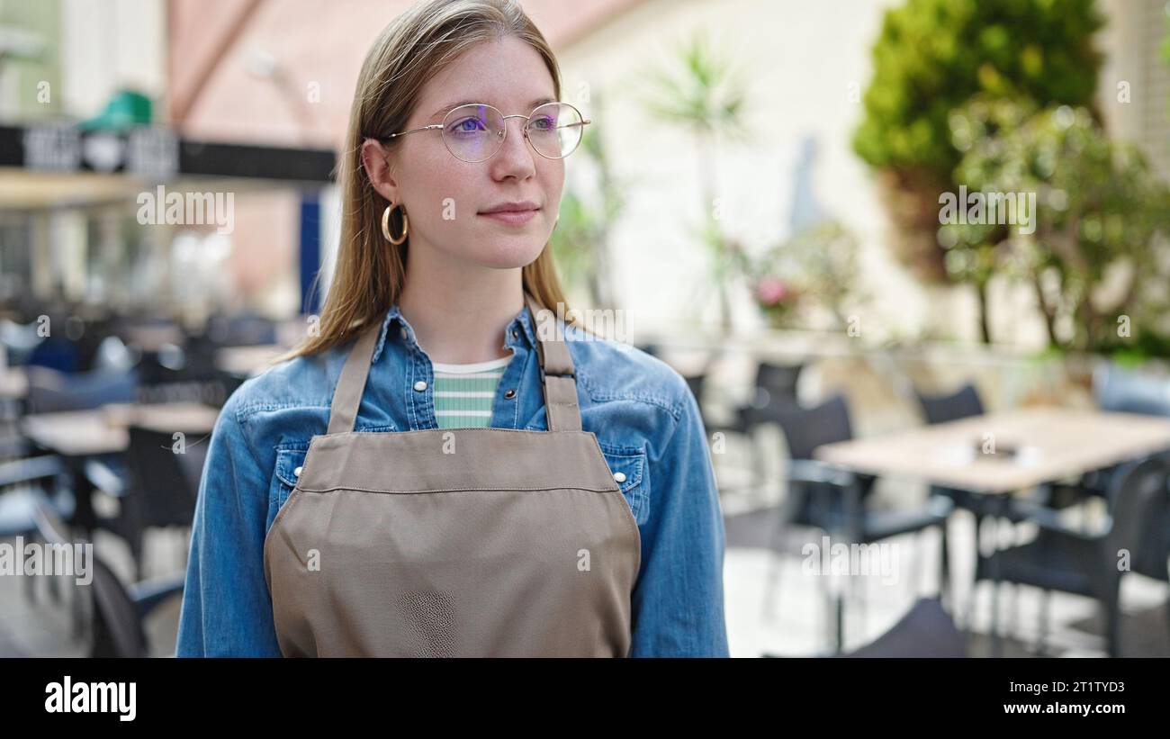 Young blonde woman waitress standing with relaxed expression at coffee ...