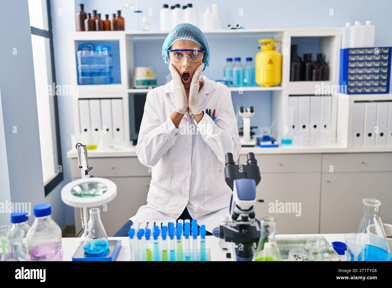 Brunette woman working at scientist laboratory afraid and shocked ...