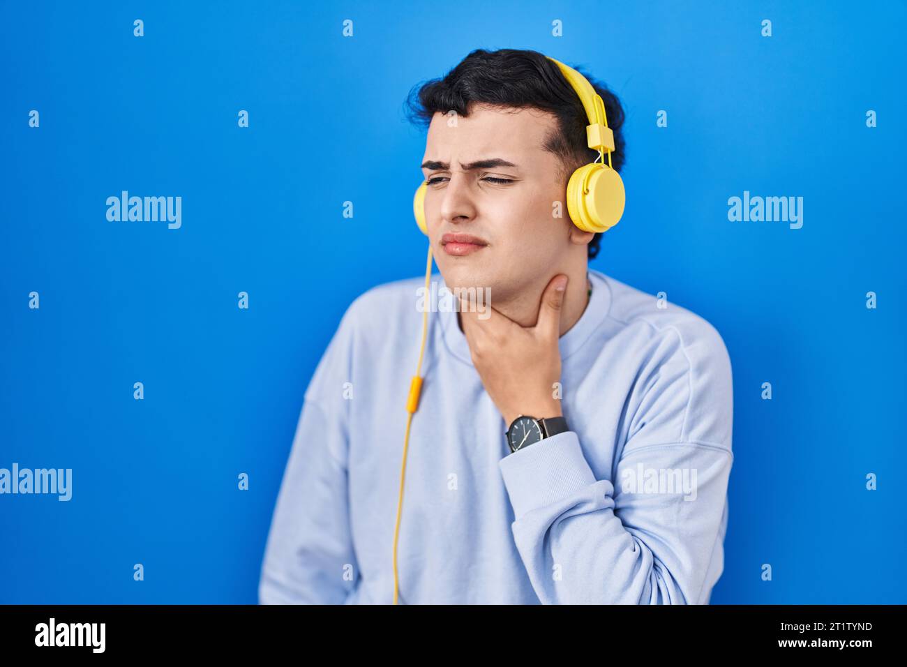 Non binary person listening to music using headphones touching painful ...