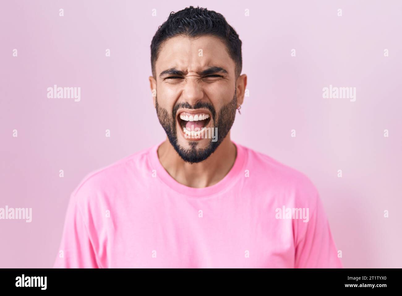 Hispanic young man standing over pink background angry and mad ...