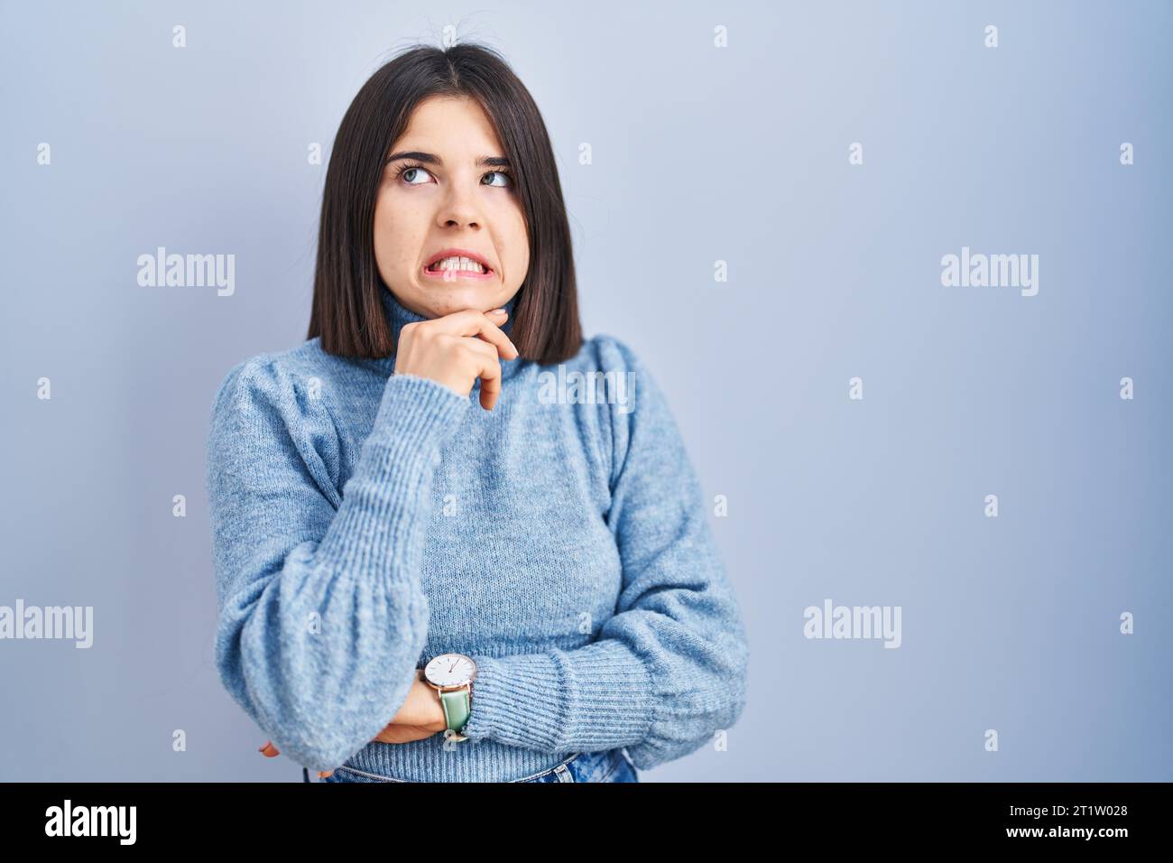 Young hispanic woman standing over blue background thinking worried ...