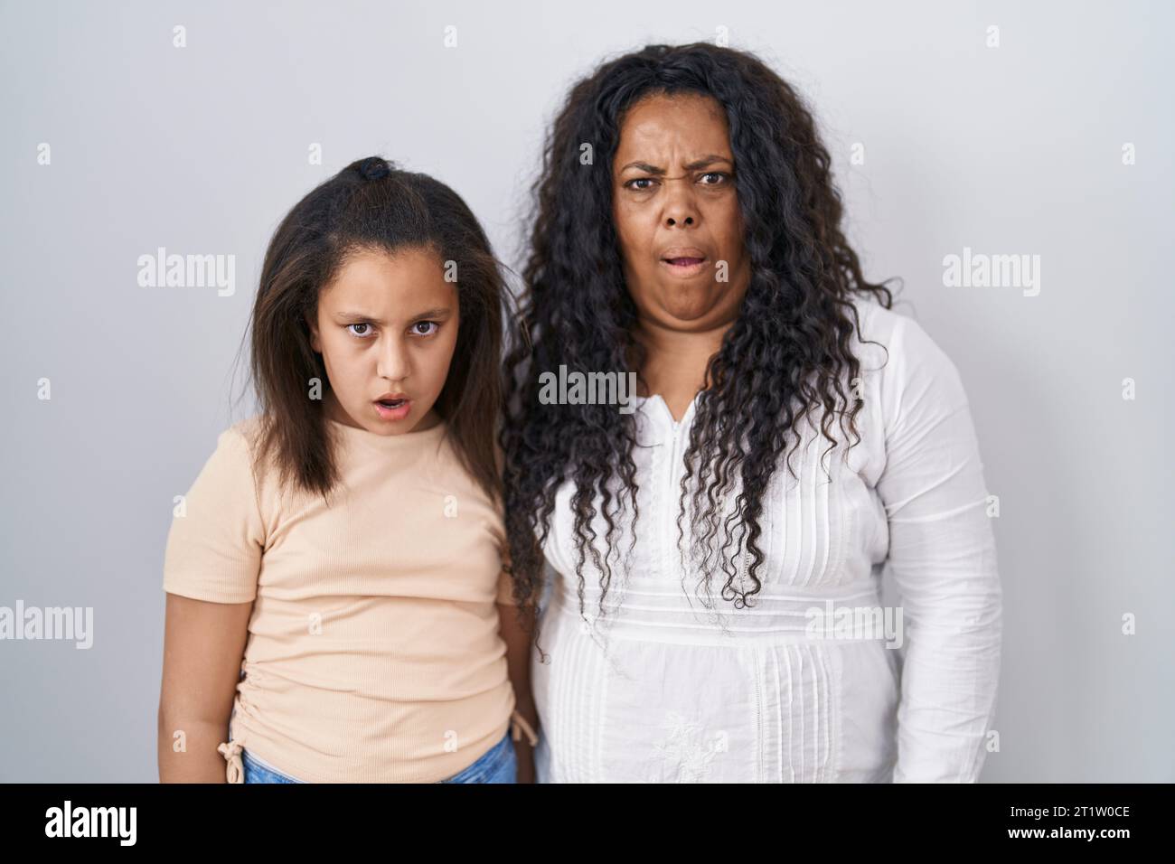 Mother and young daughter standing over white background in shock face ...