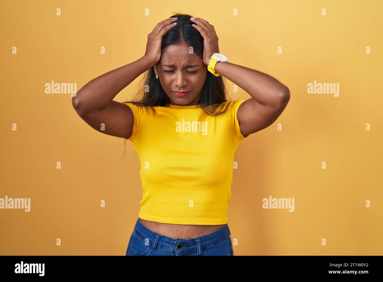 Young indian woman standing over yellow background suffering from ...
