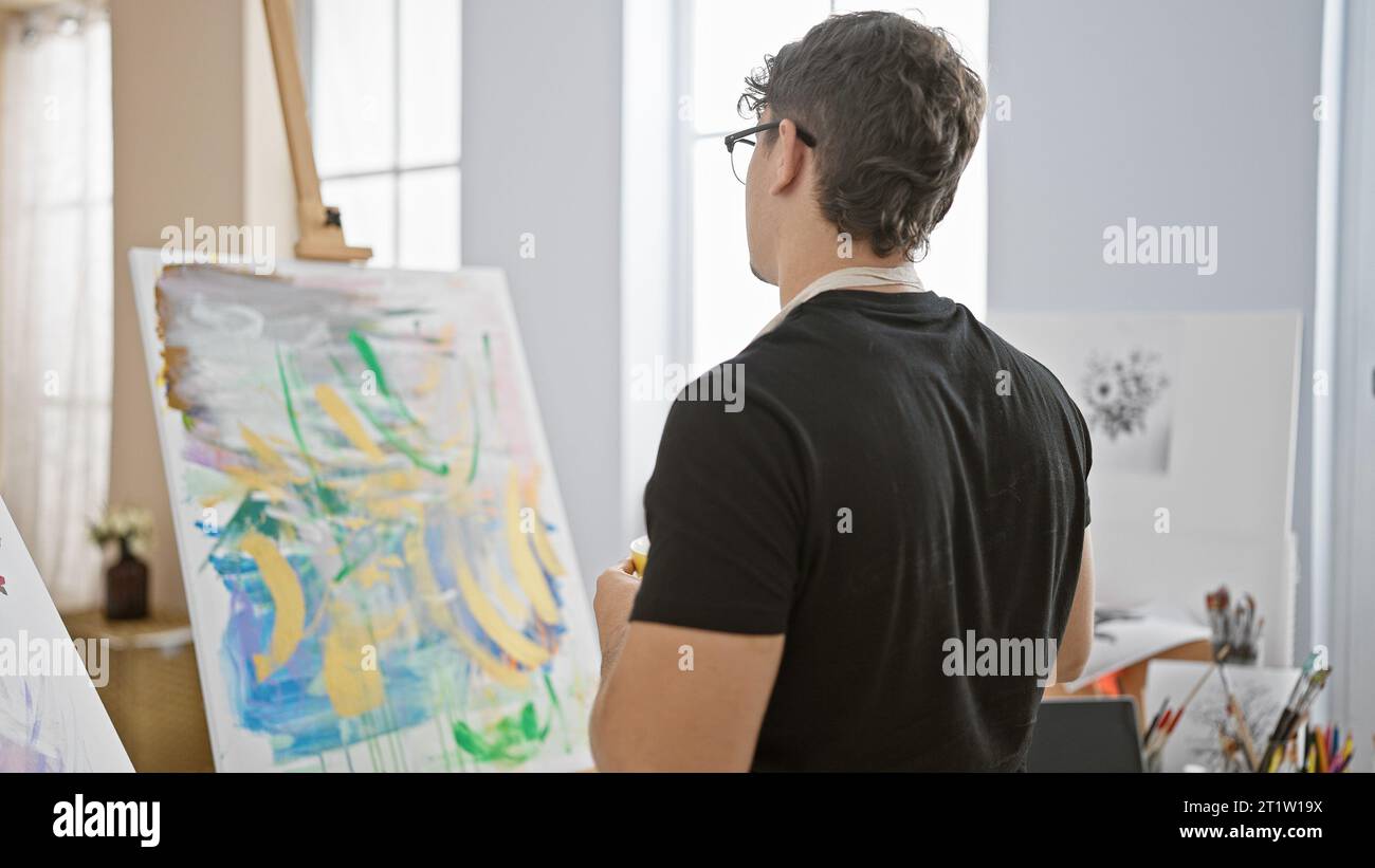 Attractive young hispanic artist, brush in hand, intently looking at ...