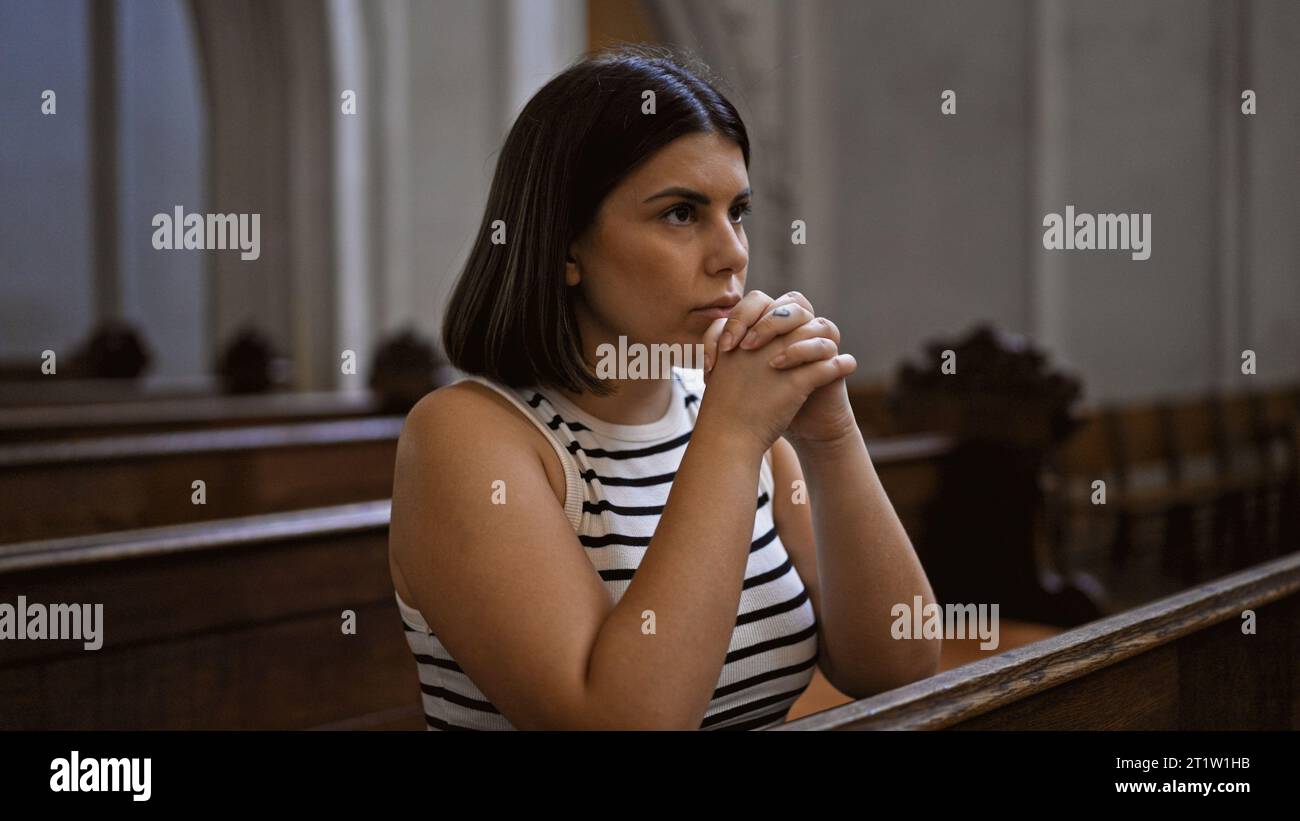 Young beautiful hispanic woman praying on a church bench at Augustinian ...
