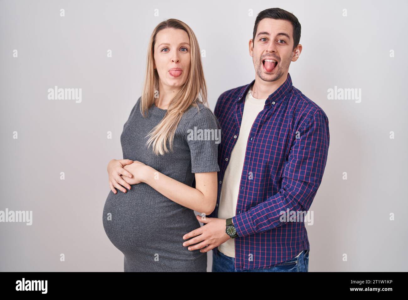 Young couple expecting a baby standing over white background sticking ...