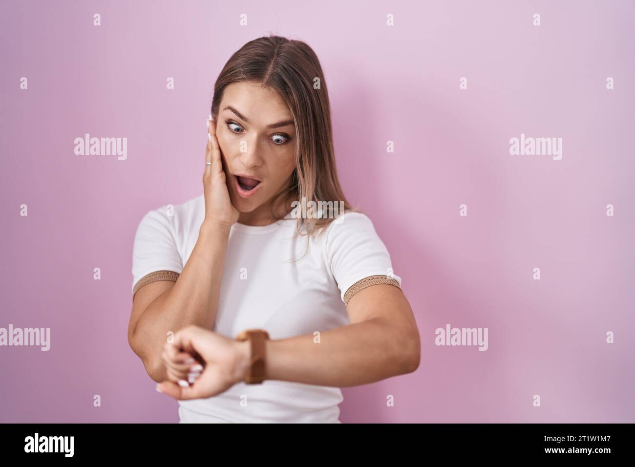 Blonde caucasian woman standing over pink background looking at the ...