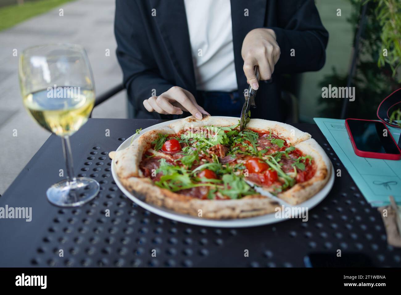 Close-up of caucasian woman client hand cutting pizza with tomatoes ...