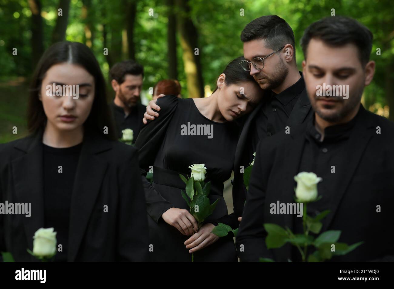 Funeral ceremony. Sad people with white rose flowers mourning outdoors ...