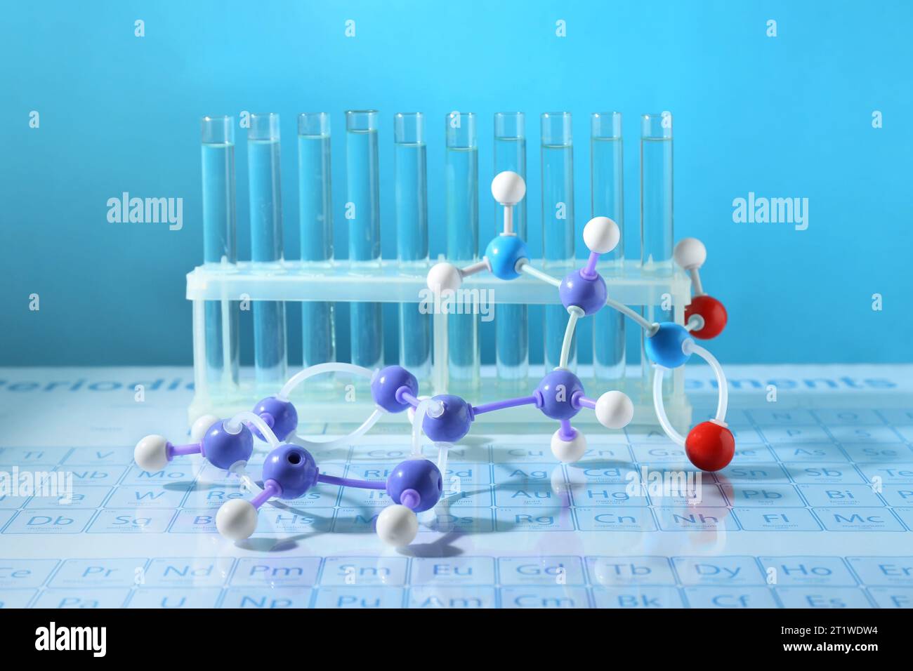 Molecular model and test tubes on periodic table against light blue ...
