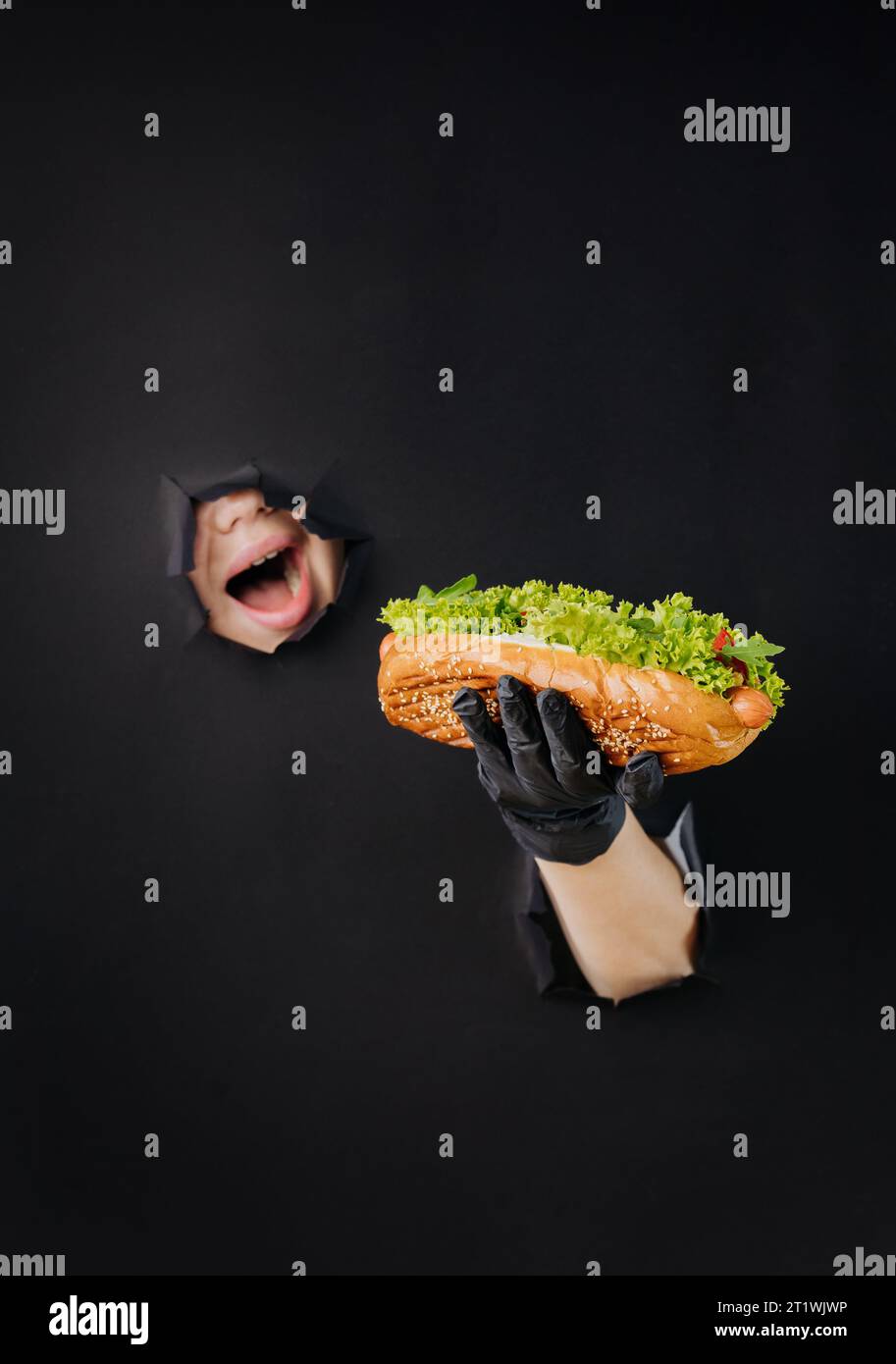 Female hand holding hot dog and looks through holes in black paper ...
