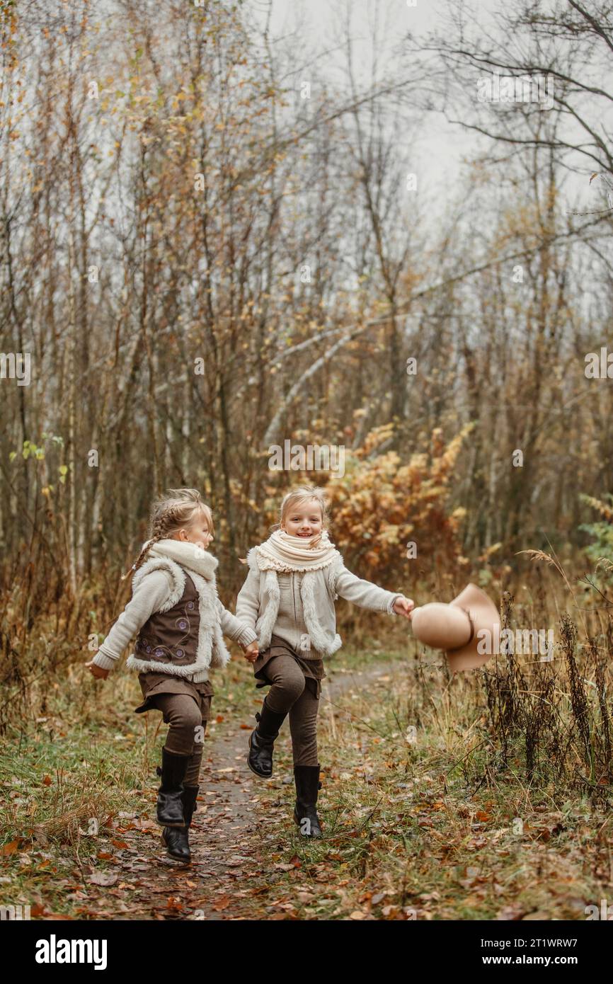 Twin girls play in the autumn park, throw their hats up. Horizontal ...