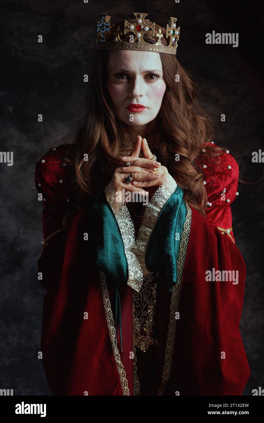medieval queen in red dress with white makeup and crown on dark gray ...