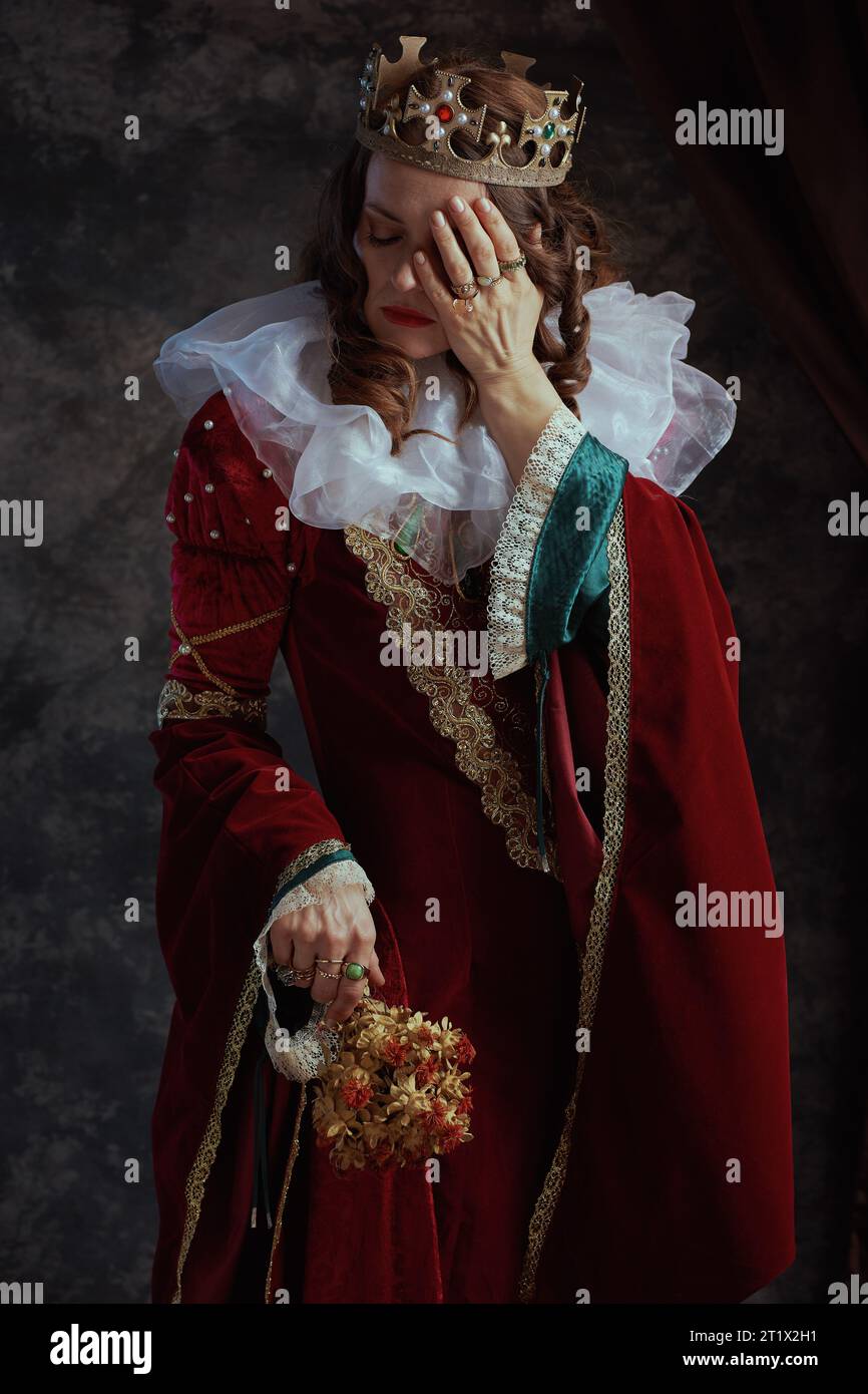 unhappy medieval queen in red dress with dried flower, white collar and ...