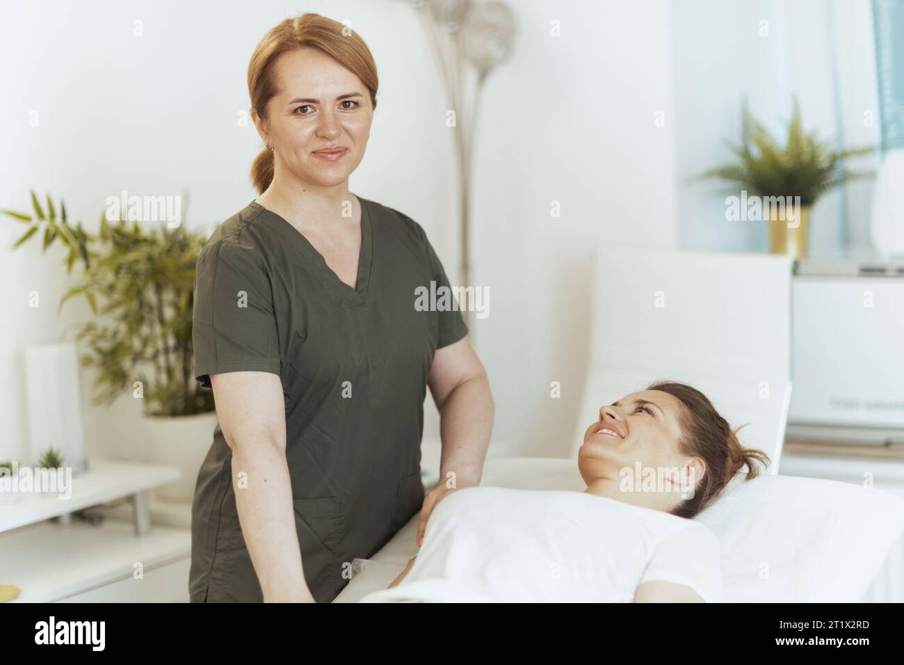 Healthcare time. smiling female massage therapist in massage cabinet with client conducting ...