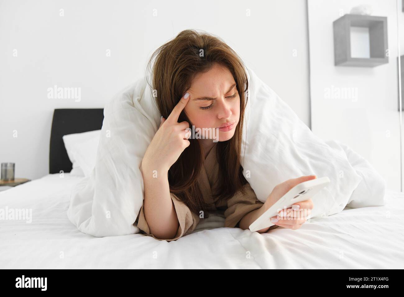 Woman with confused face, waking up in morning and checking her mobile ...