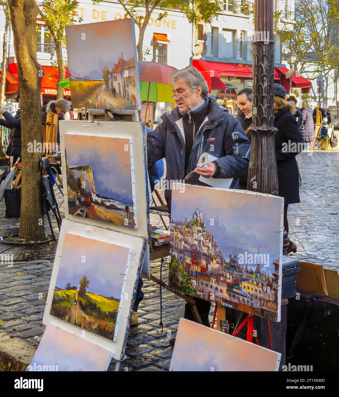 A male artist at work painting a picture on canvas on an easel outdoors ...