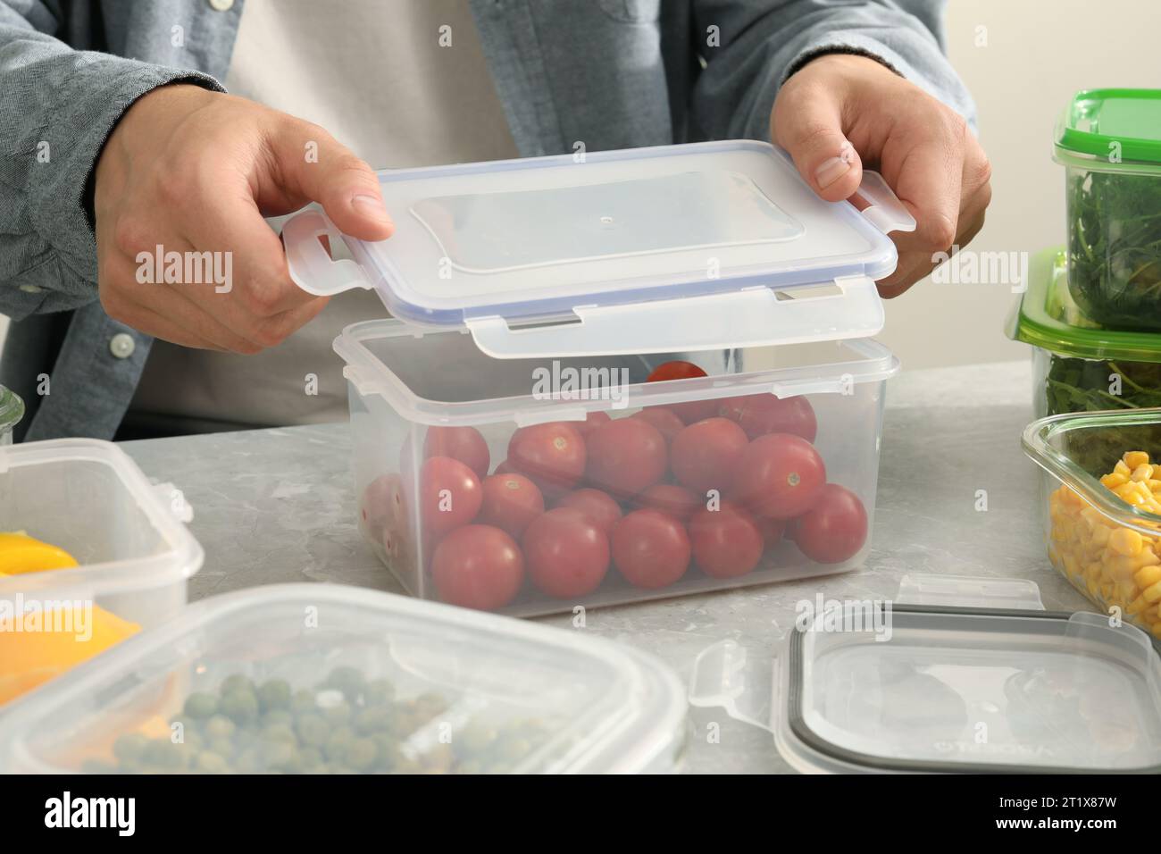 Man closing plastic container with lid at light grey marble table in ...