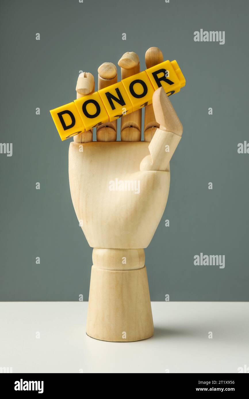 Mannequin hand holding word Donor made of cubes on white table against ...