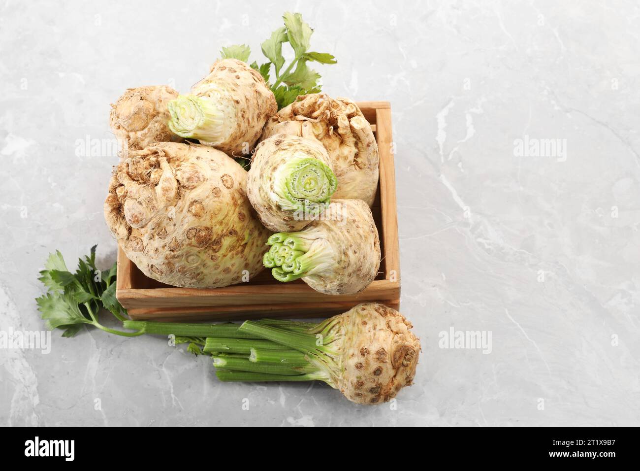 Fresh raw celery roots and wooden crate on light grey table, above view ...