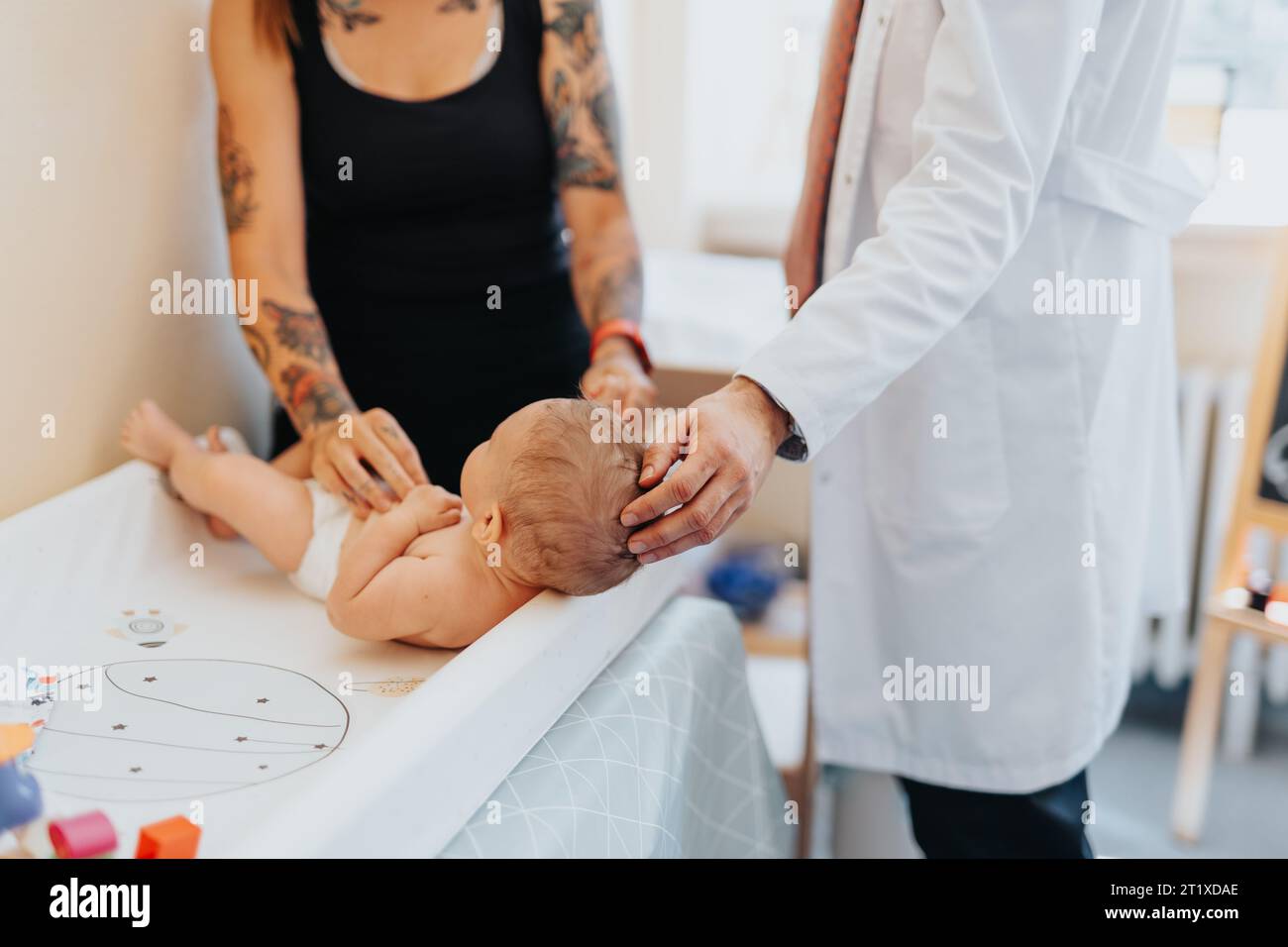Male pediatrician caressing baby's head while his mom is changing her ...