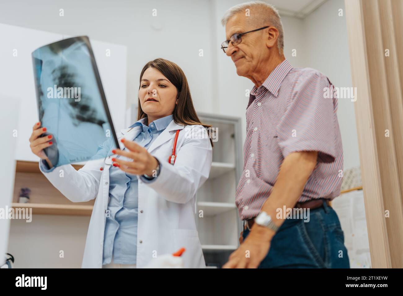 Doctor carefully examines x-ray film of elderly patient's lungs in office. Expert consultation ...