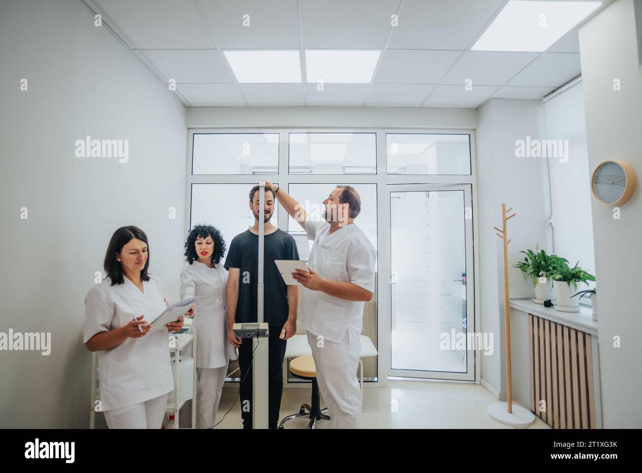 Three doctors measuring young patient height using metric scale at the ...