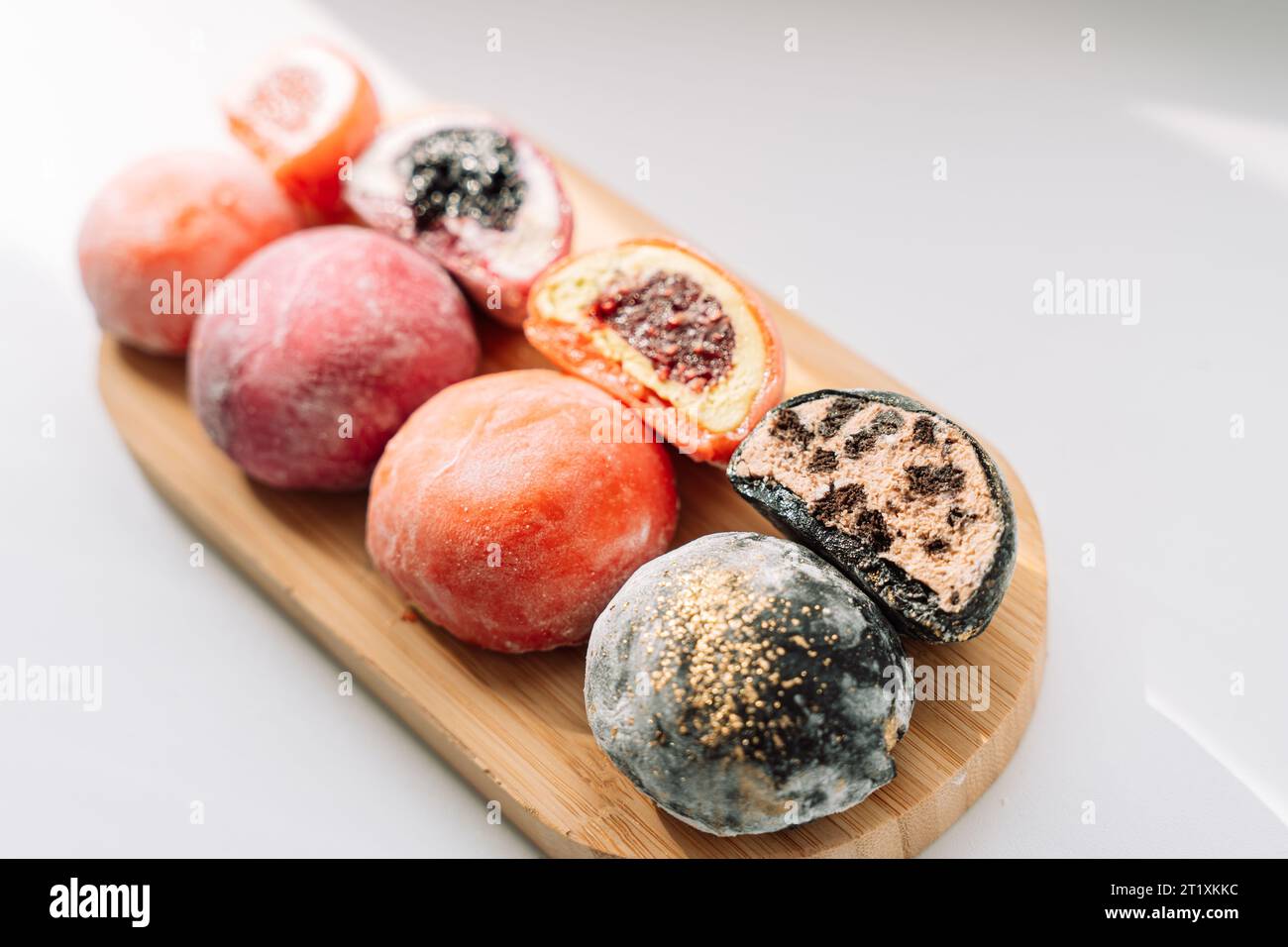 Whole and cut colored mochi on a wooden board on a white background ...