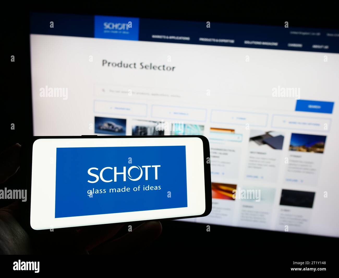 Person holding mobile phone with logo of German glass manufacturing company Schott AG in front ...
