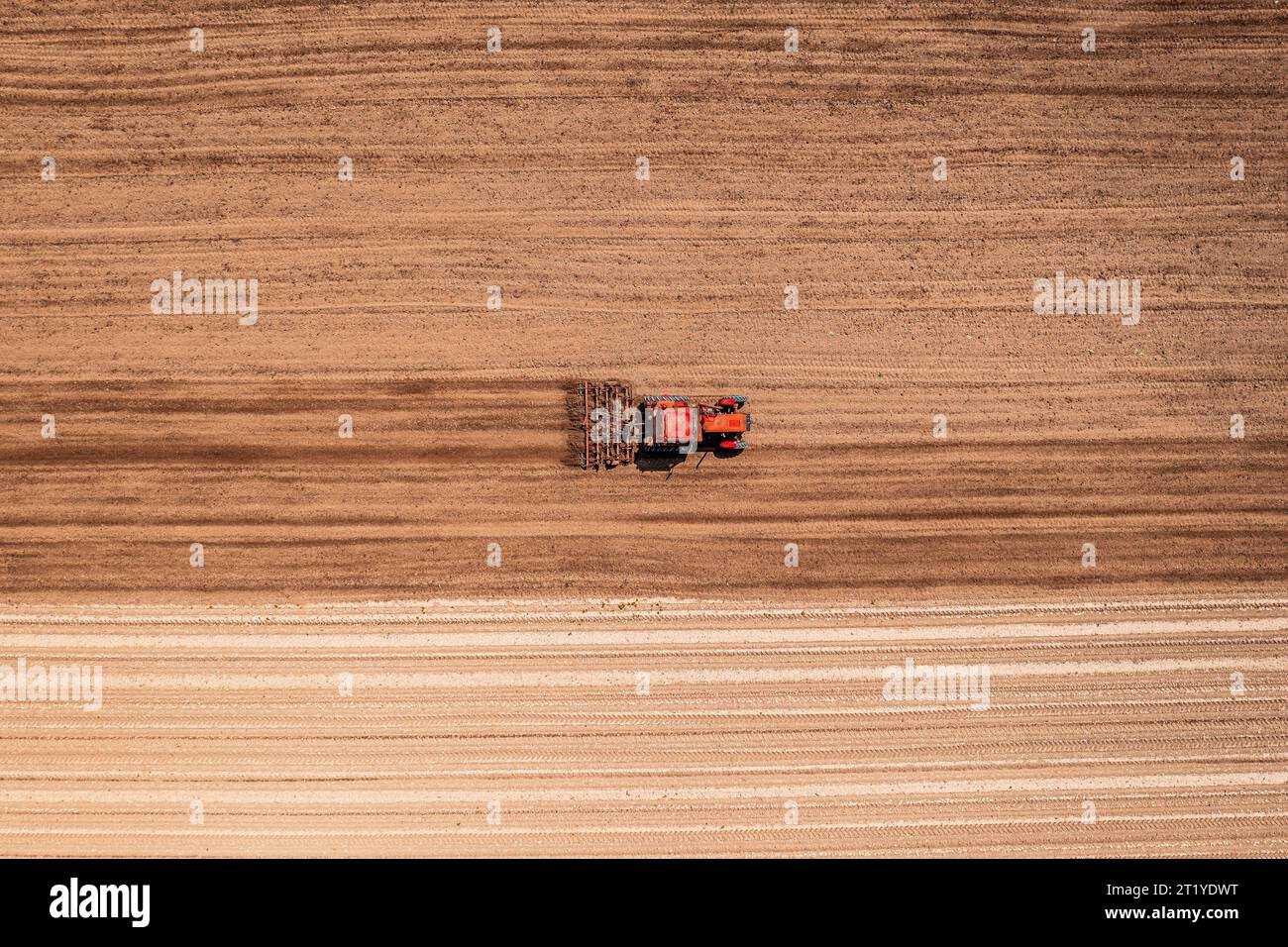 Red agricultural tractor with tiller attached performing field tillage ...