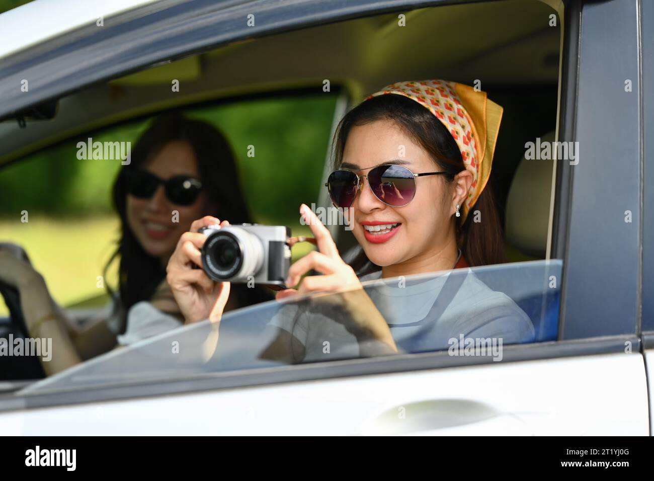 Smiling young woman taking photos from a car window with vintage retro ...
