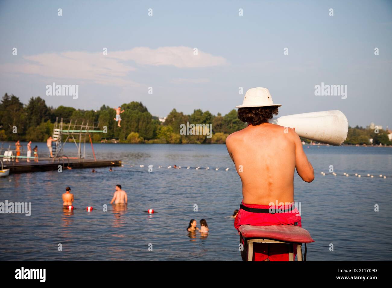 A lifeguard watches over swimmers as they jump off the diving board and ...