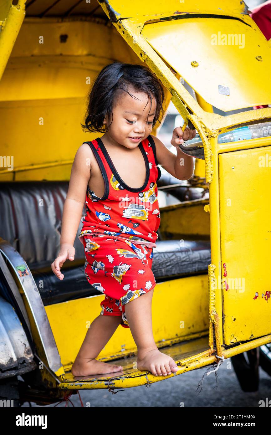 A cute Filipino girl plays on her fathers tricycle, pedicab or rickshaw ...