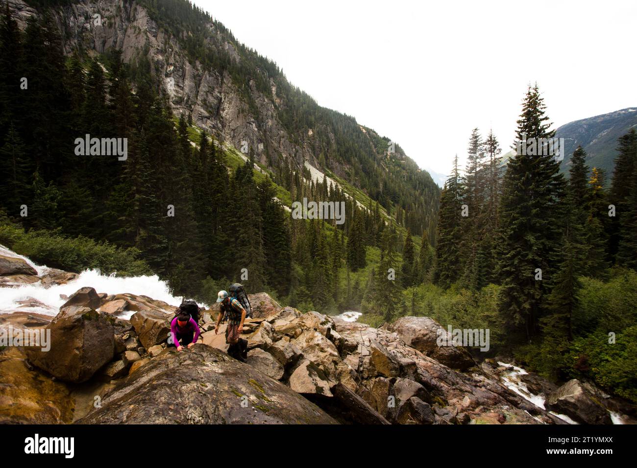 Hikers climb rocks alongside a waterfall in Washington's North Cascades ...