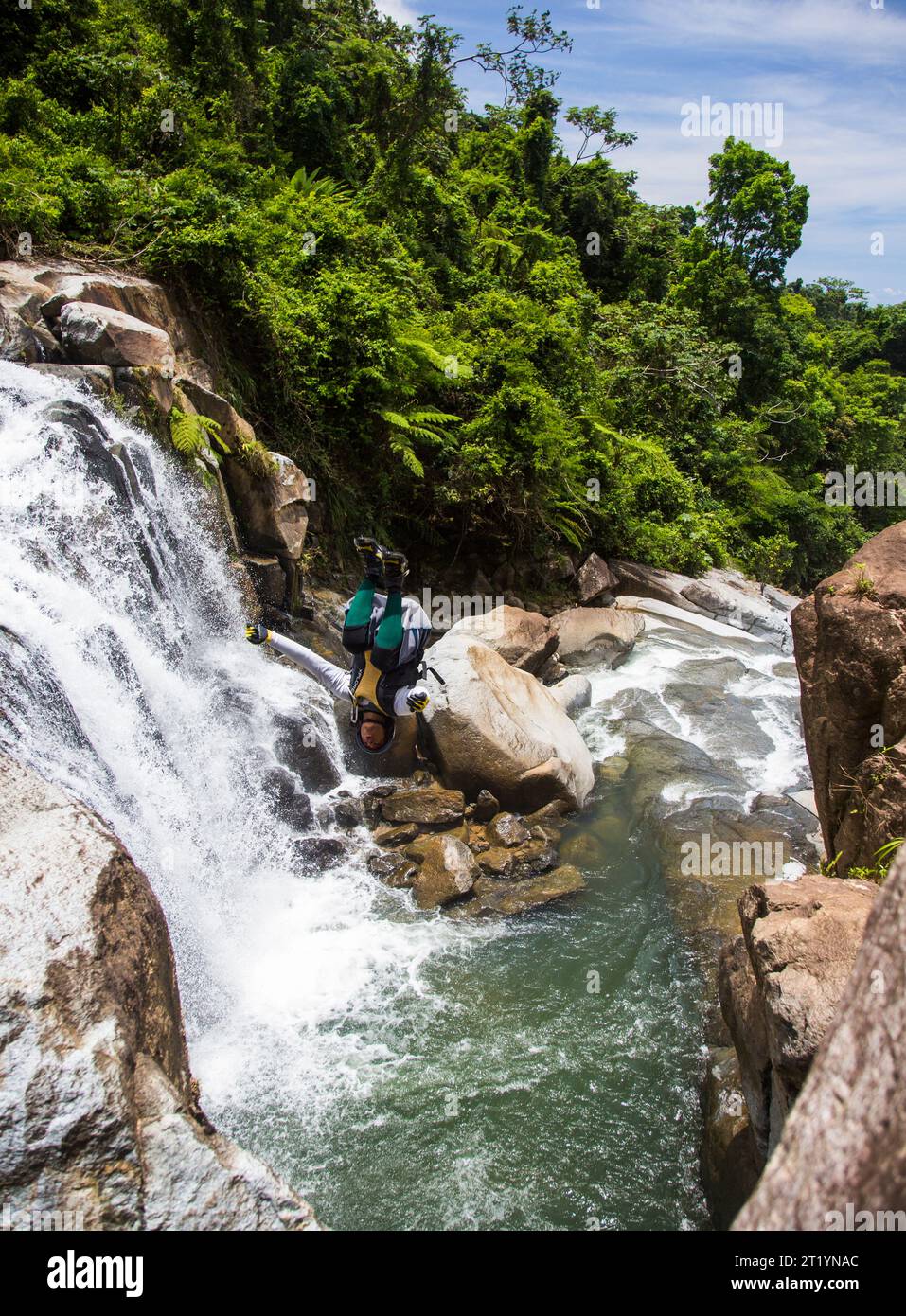 A young man does a back flip into a swimming hole during a river ...