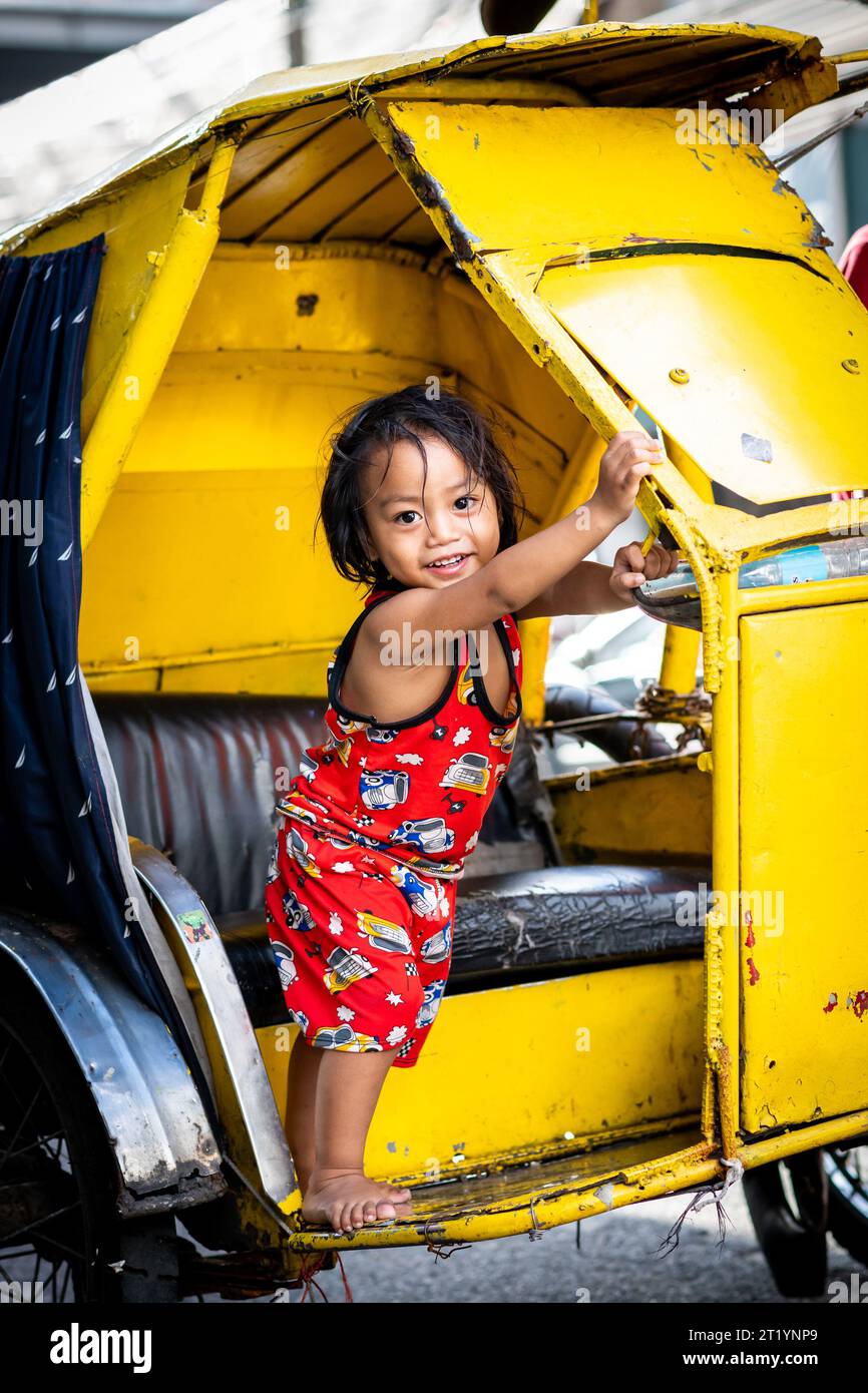 A cute Filipino girl plays on her fathers tricycle, pedicab or rickshaw ...