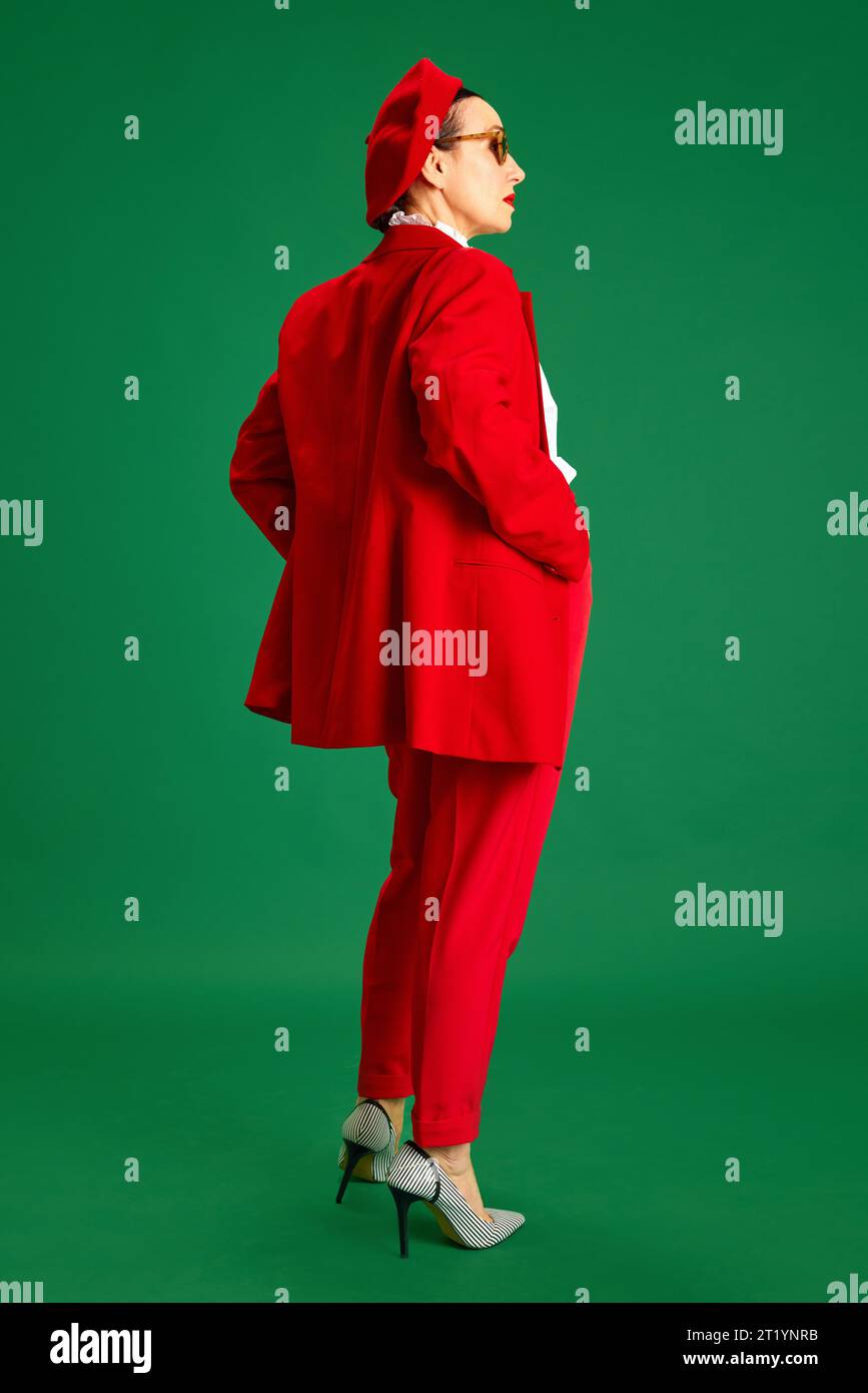 Side view of elegant woman in her 60s, wearing stylish, bright red suit ...