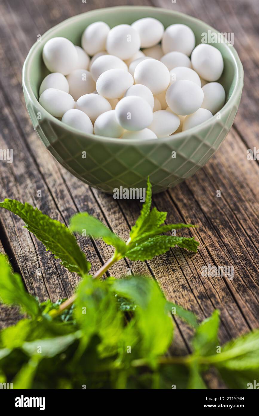 Mint candies in bowl. Menthol bonbons and mint leaves on the wooden ...