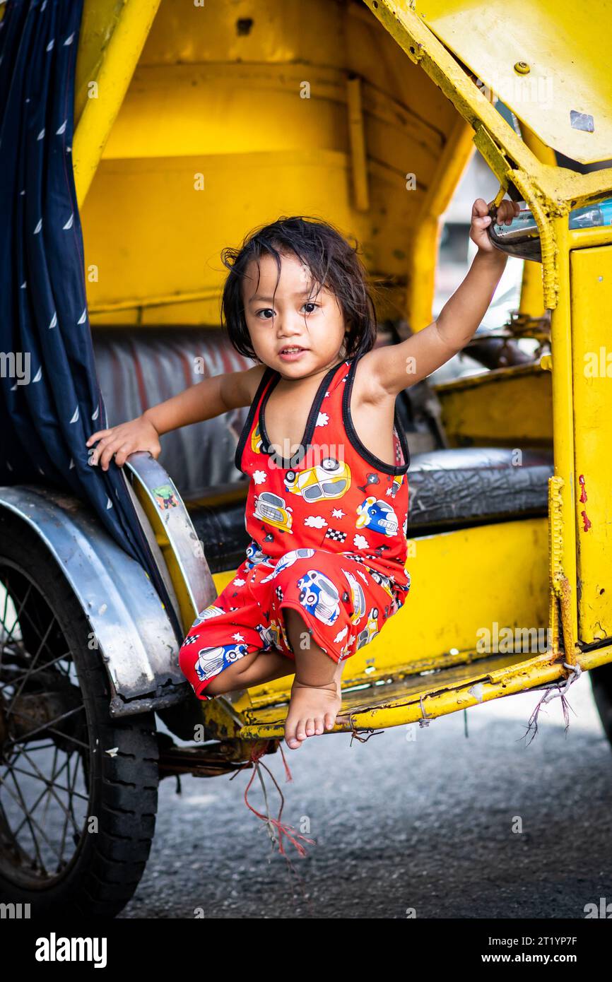 A cute Filipino girl plays on her fathers tricycle, pedicab or rickshaw ...