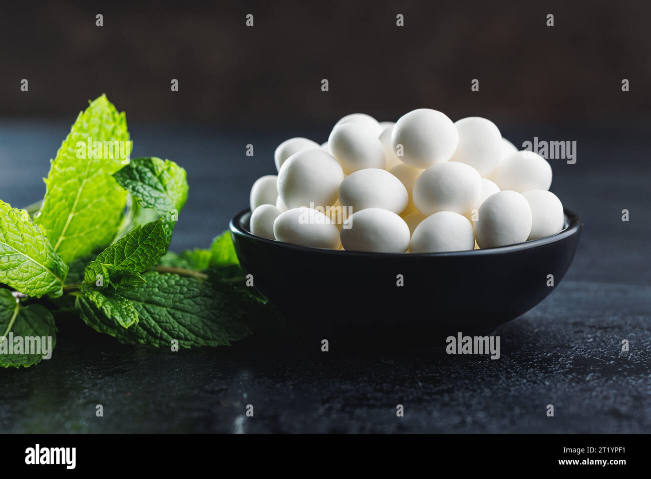 Mint candies in bowl. Menthol bonbons and mint leaves on the black ...