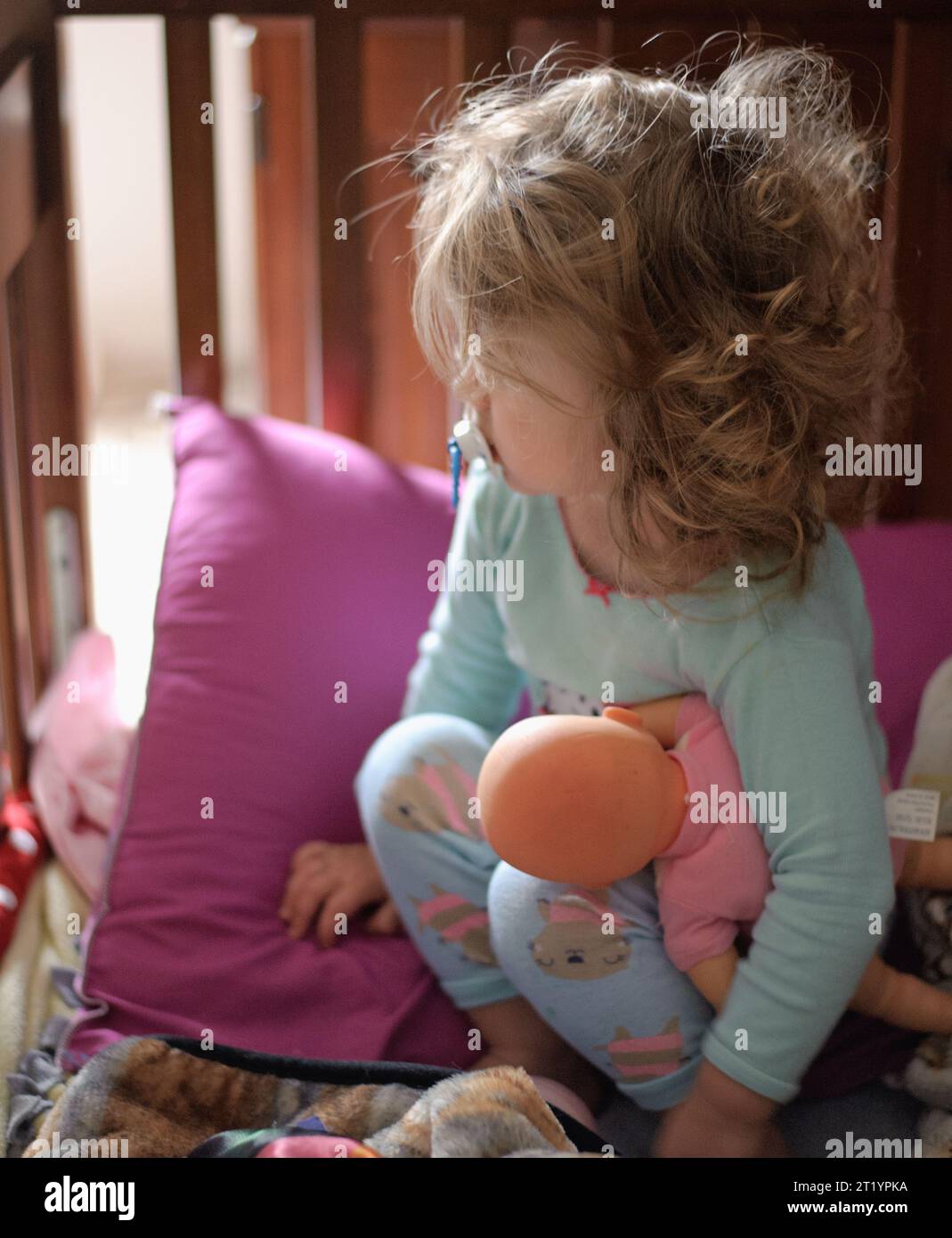 Toddler with pacifier holding baby doll in brown crib Stock Photo - Alamy