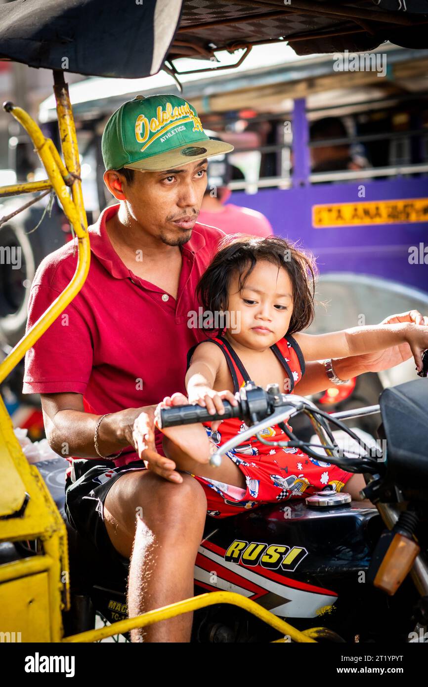 A Filipino father plays with his cute daughter sat on his tricycle ...