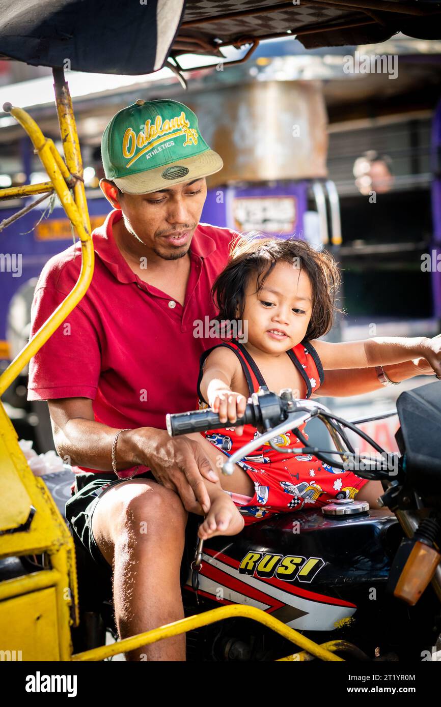 A Filipino father plays with his cute daughter sat on his tricycle ...