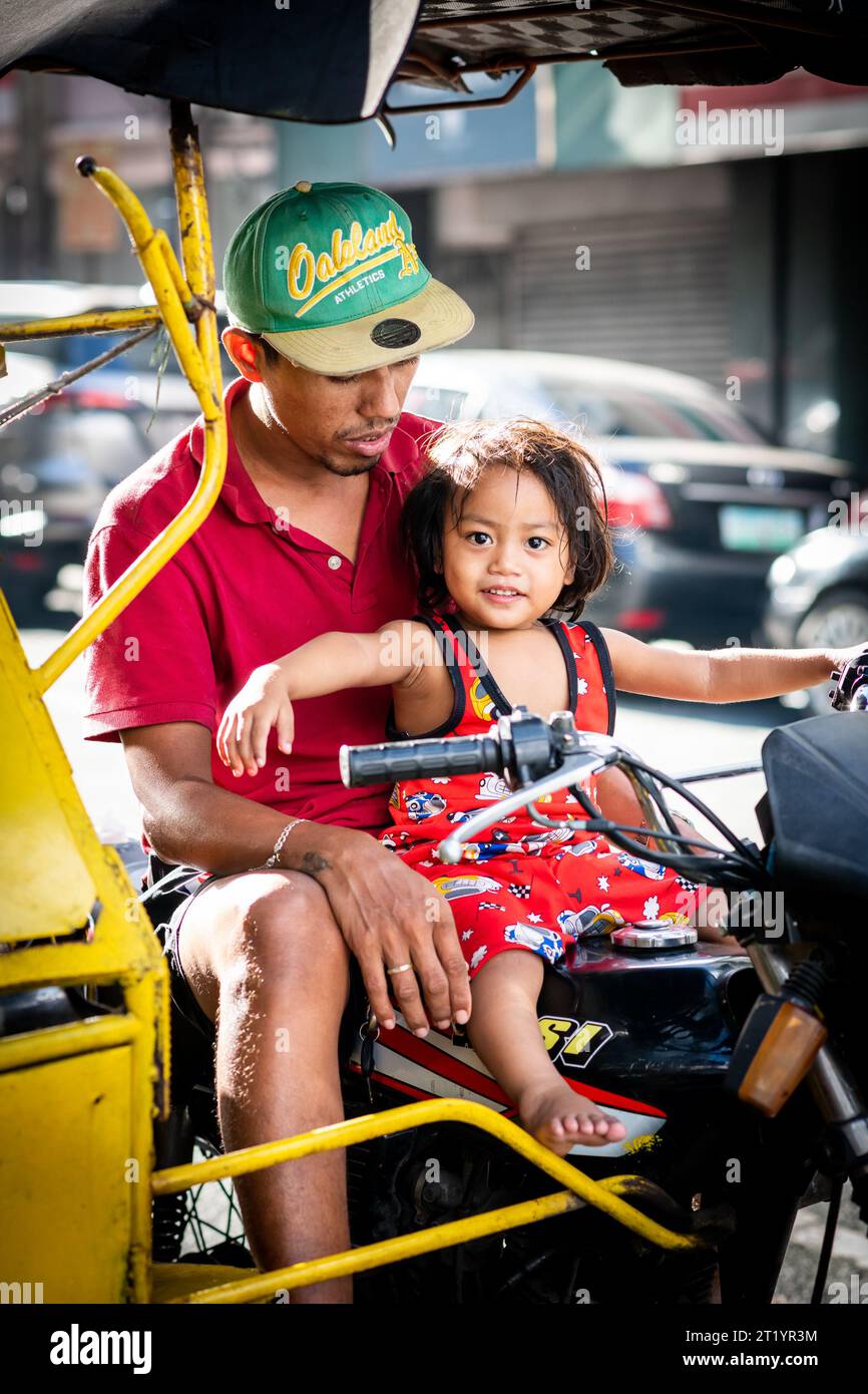 A Filipino father plays with his cute daughter sat on his tricycle ...