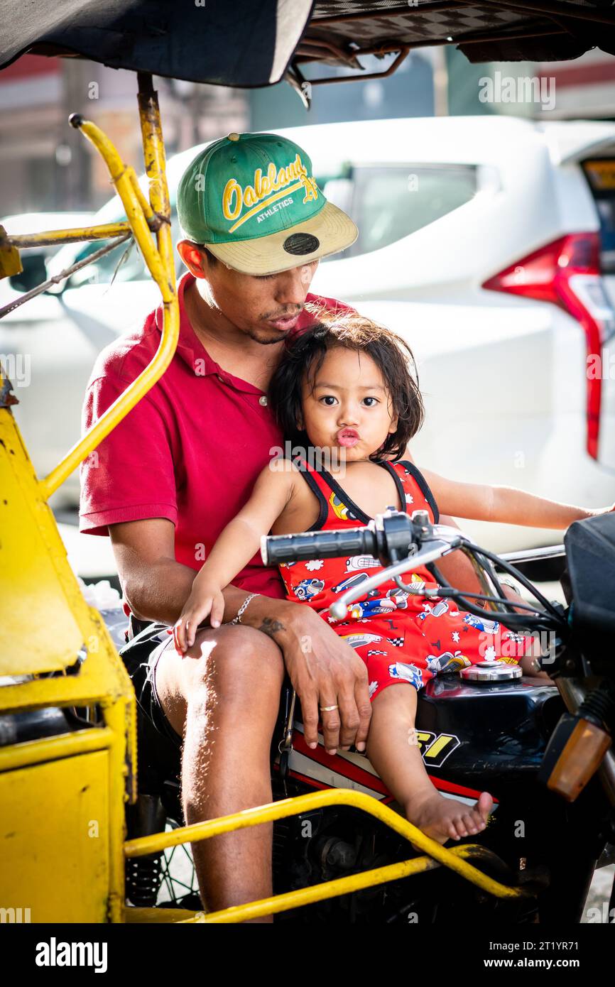 A Filipino father plays with his cute daughter sat on his tricycle ...